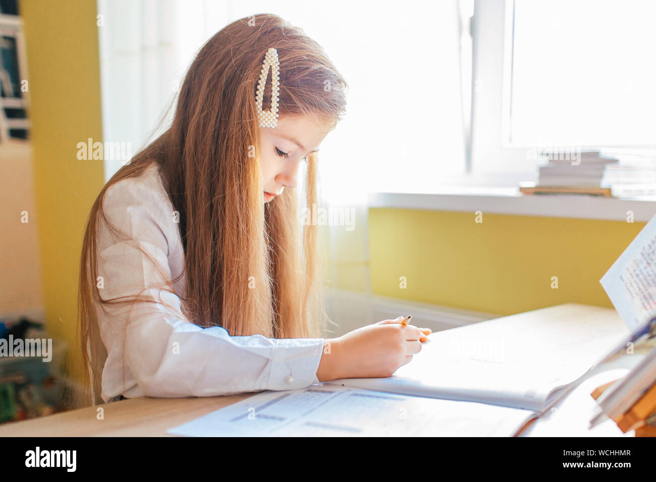 Education at home concept - Cute little girl with long hair studying or completing home work on ...