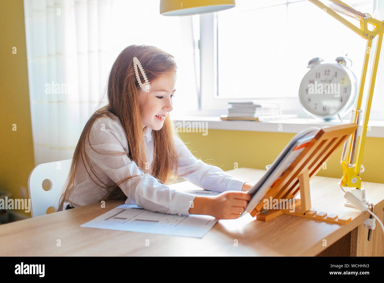 Education at home concept - Cute little girl with long hair studying or completing home work on ...