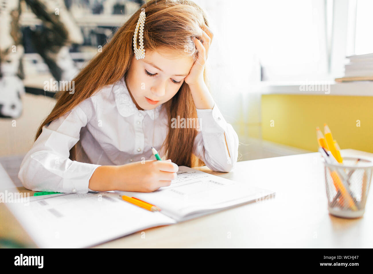Education at home concept - Cute little girl with long hair studying or completing home work on ...