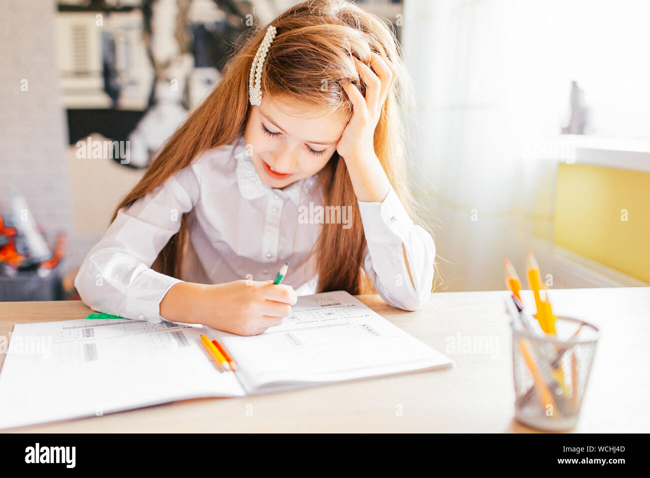 Education at home concept - Cute little girl with long hair studying or completing home work on ...