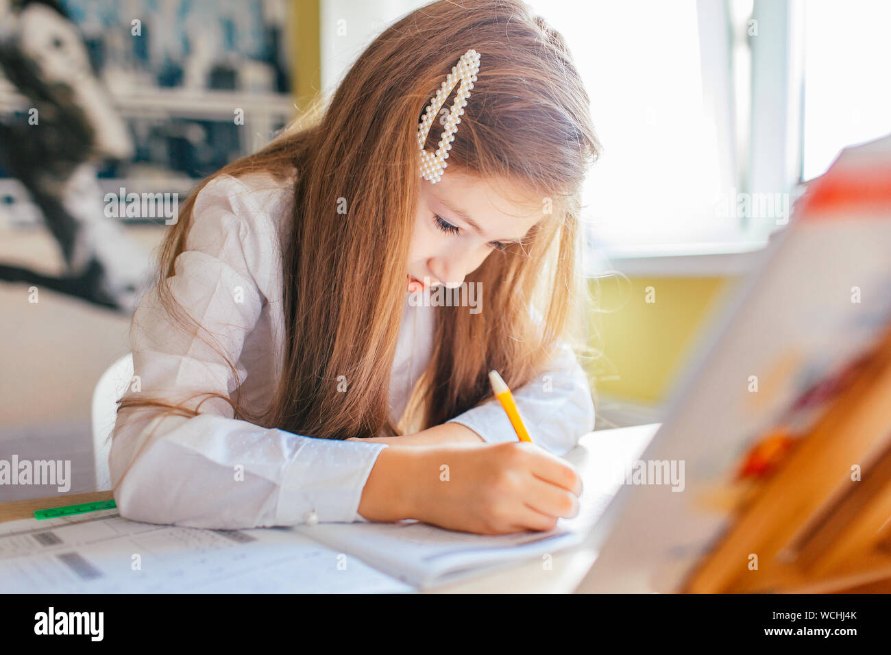 Education at home concept - Cute little girl with long hair studying or completing home work on ...