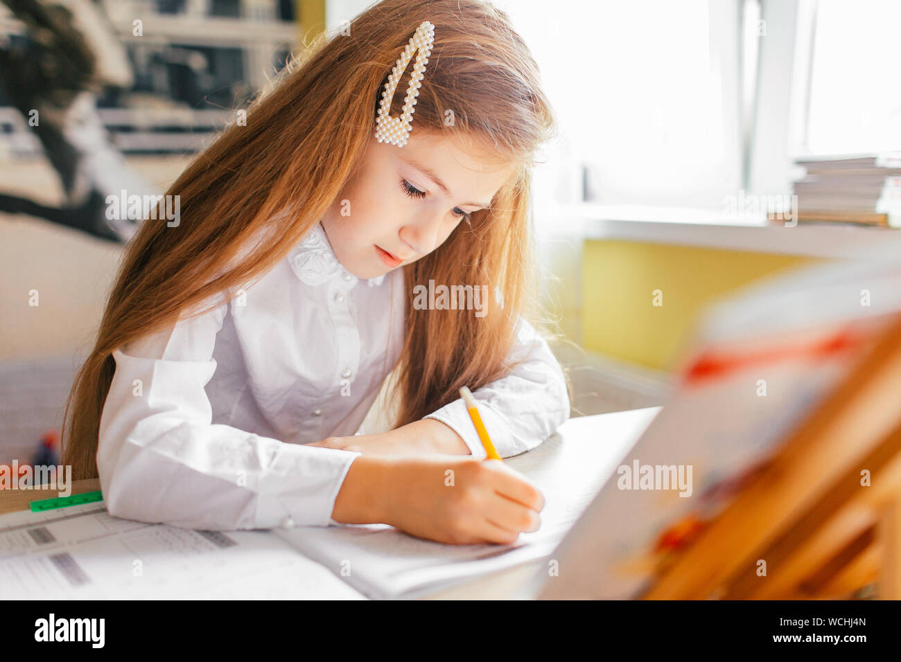 Education at home concept - Cute little girl with long hair studying or completing home work on ...
