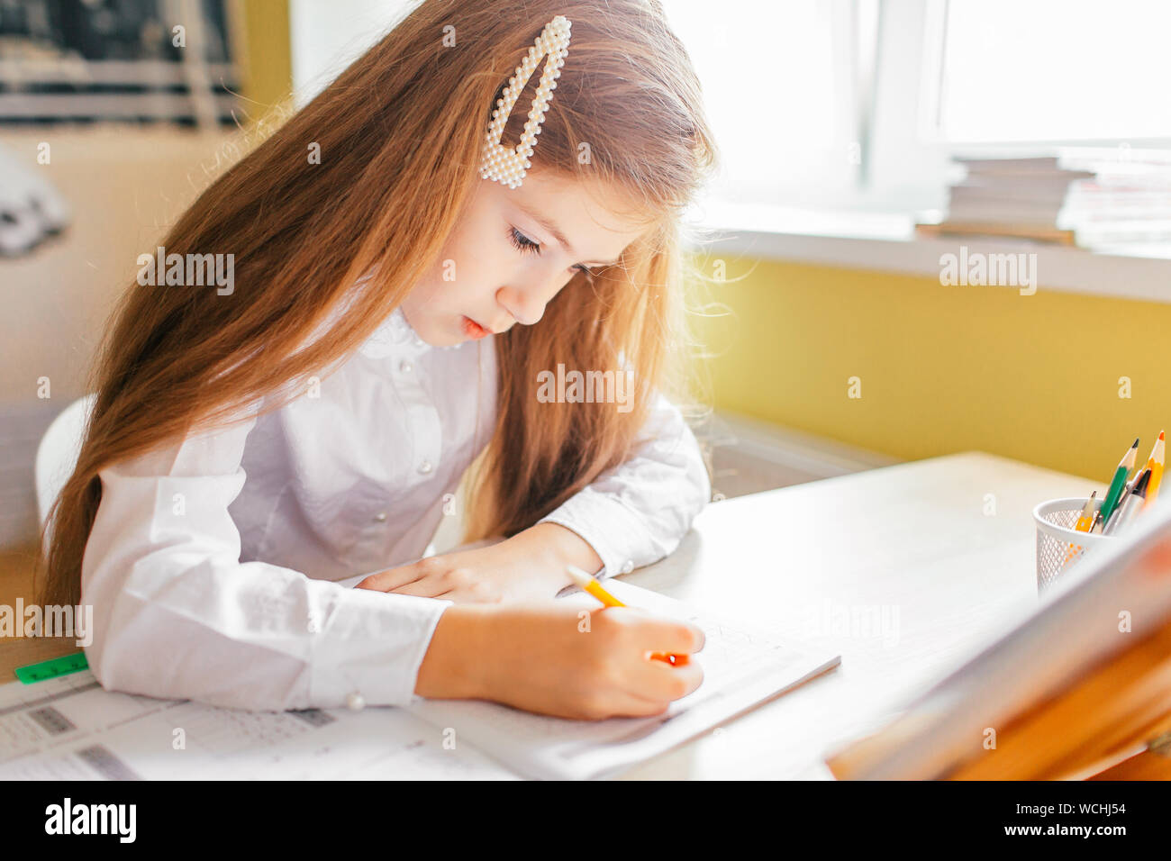 Education at home concept - Cute little girl with long hair studying or completing home work on ...