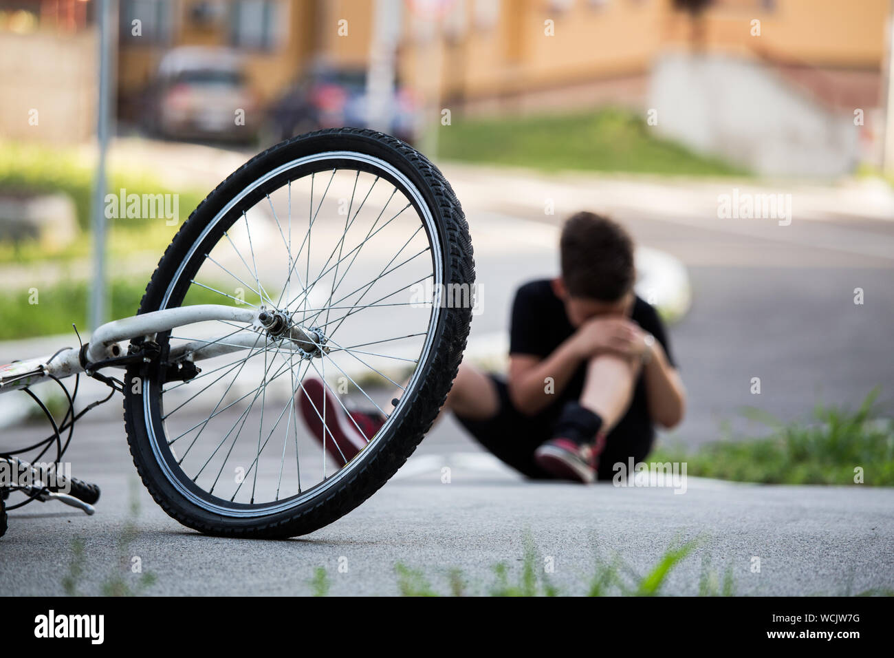 Boy in the street ground with a knee injury screaming after falling off ...