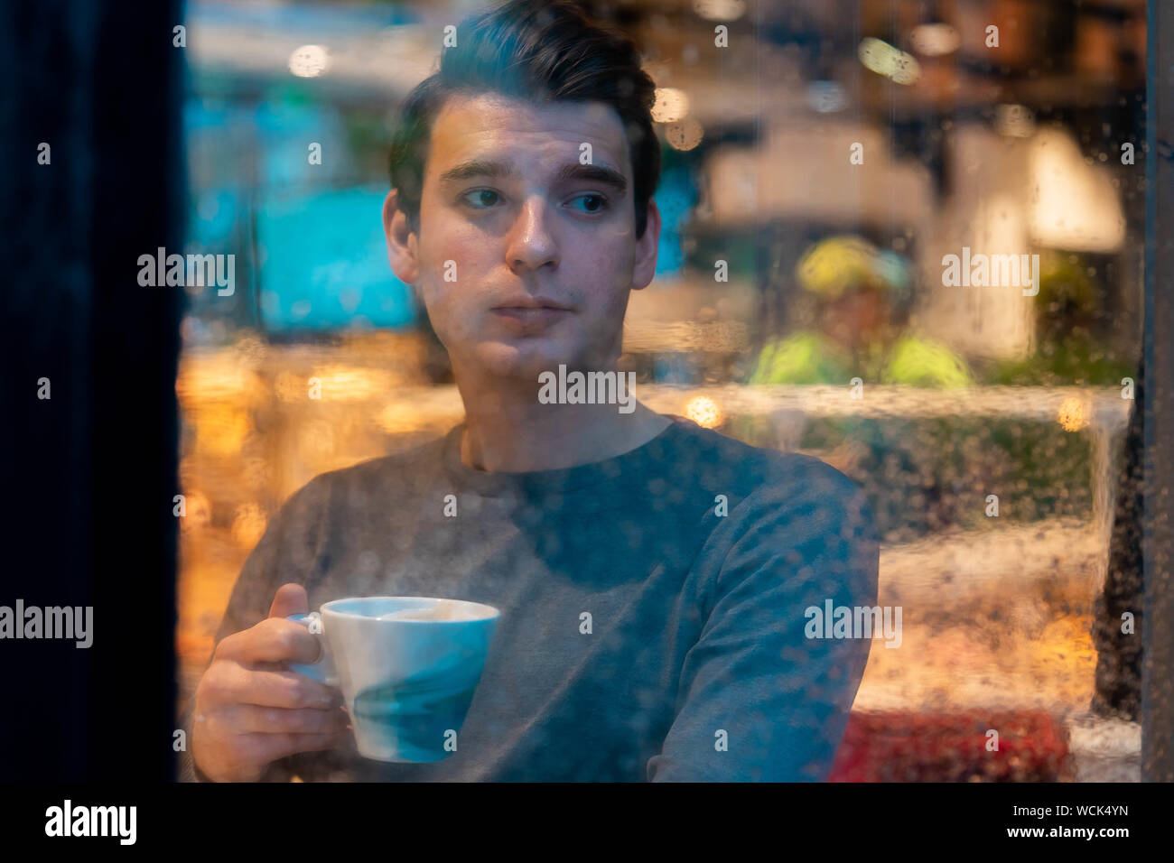 Young pensive handsome man drinking tea or coffee on rainy day in cozy ...