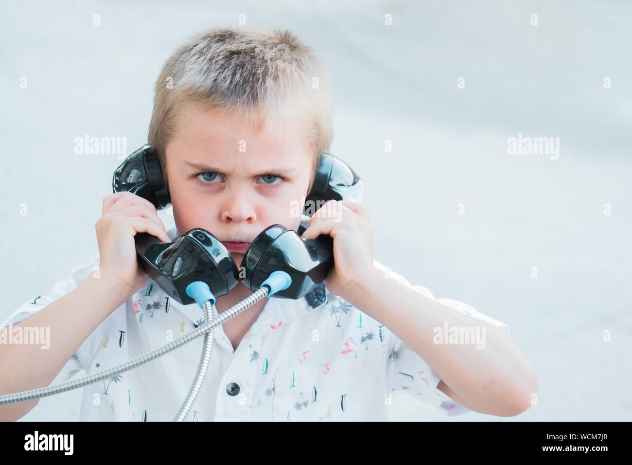 Adorable young boy holding two telephones with an angry expression on ...