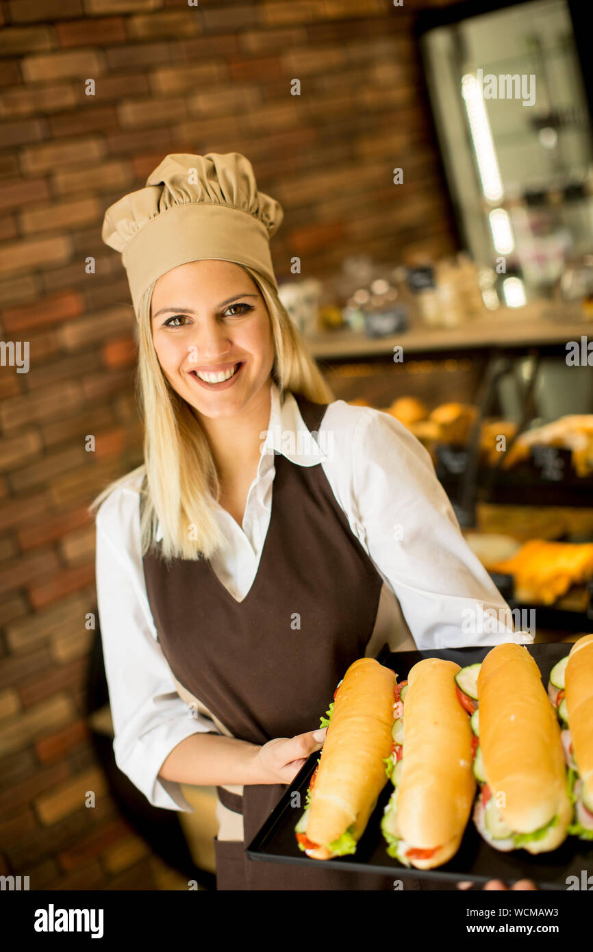 Portrait of female baker posing with various types of sandwiches in the ...