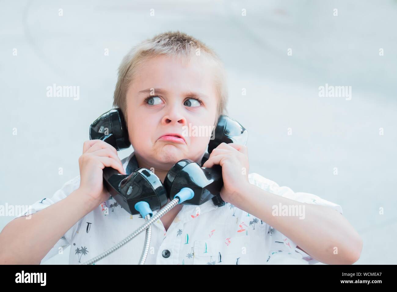 Young boy holding two black old telephones with an angry expression on ...