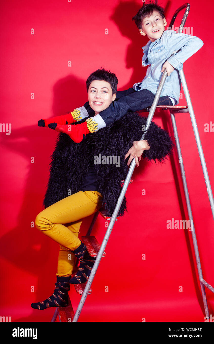 pretty young mother with little son on ladder on red background posing ...