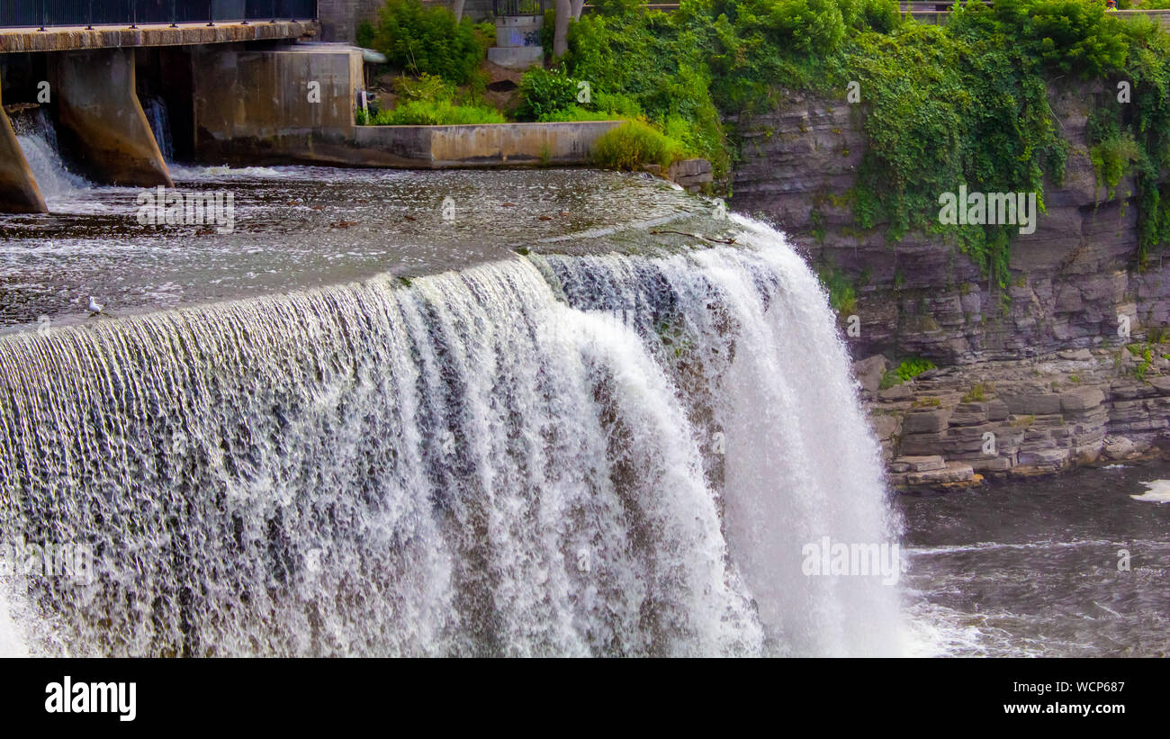 A rushing waterfall drops whitewater down a cliff, just beyond a dam ...