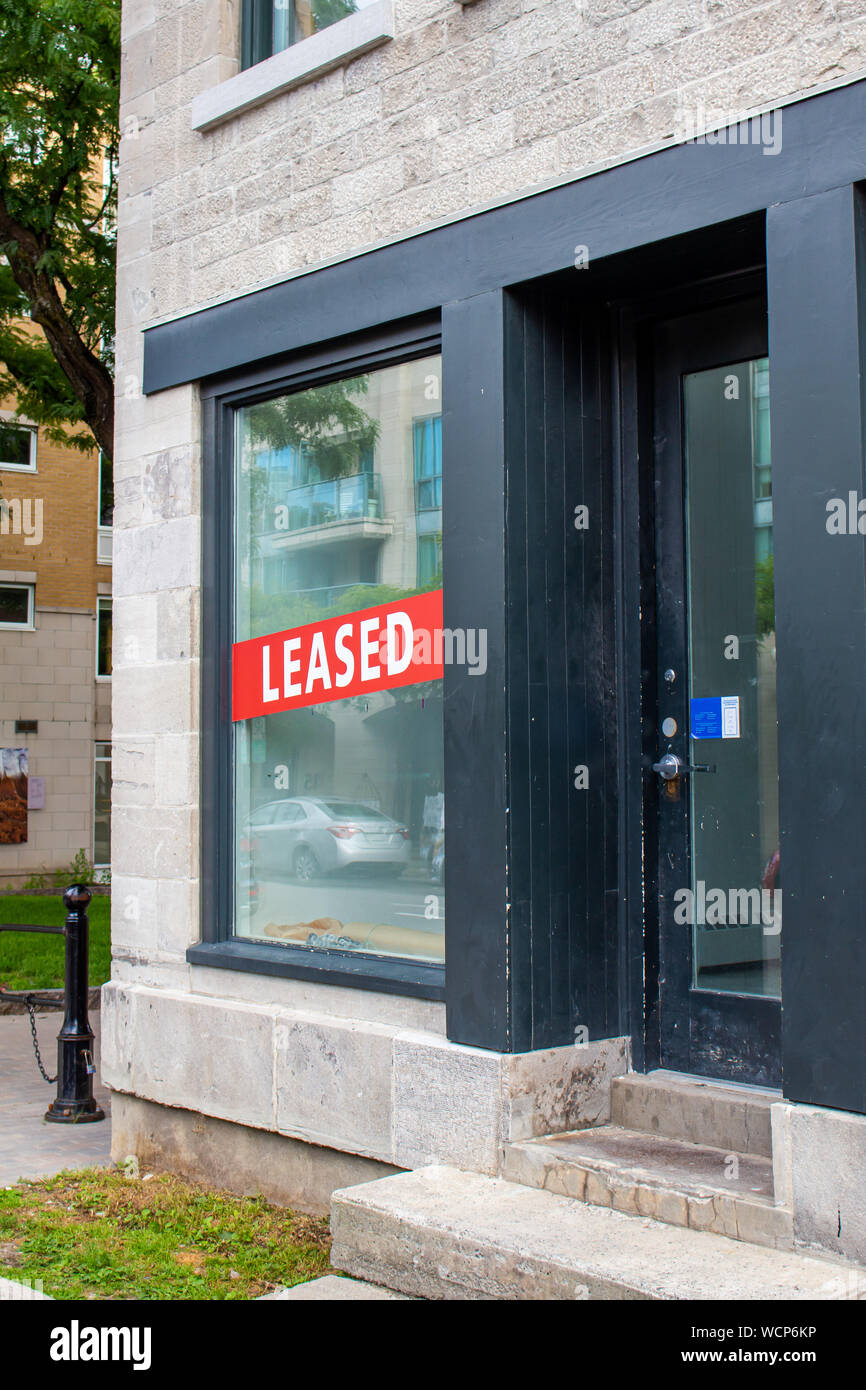The window of an empty storefront on a stone brick building shows a red ...