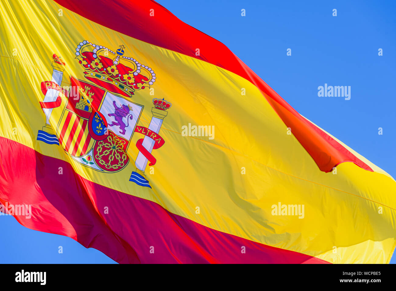 Red and yellow Spain flag with royal shield waving in the wind isolated ...