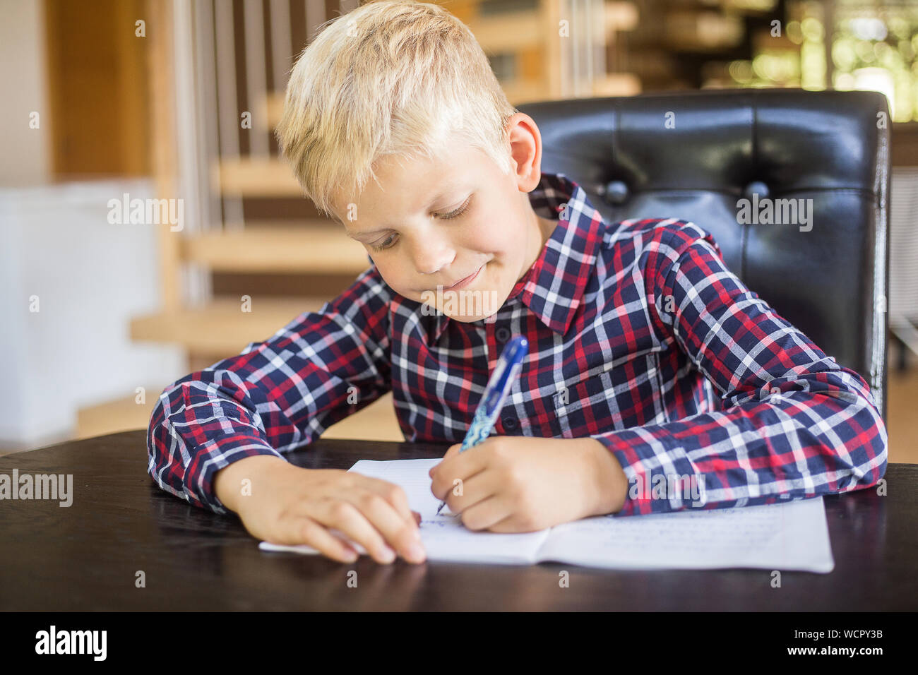 Happy schoolboy writing to notebook at home. Homework. Education ...