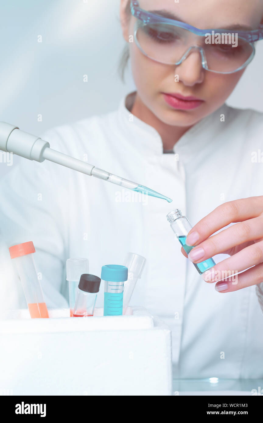 Young female scientist loads liquid sample into disposable plastic vial ...