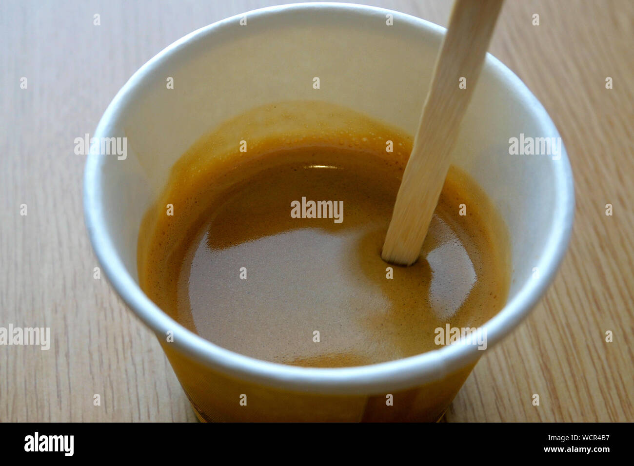 Coffee with foam mixed with a wooden stick, in a disposable paper cup ...