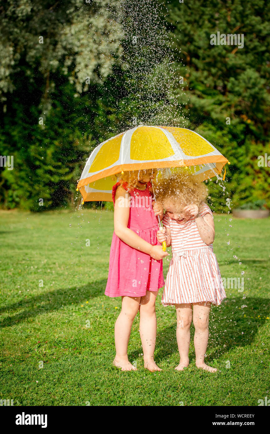 Two young girls sisters standing outdoors in garden under umbrella with ... Two young girls sisters standing outdoors in garden under umbrella with ...
