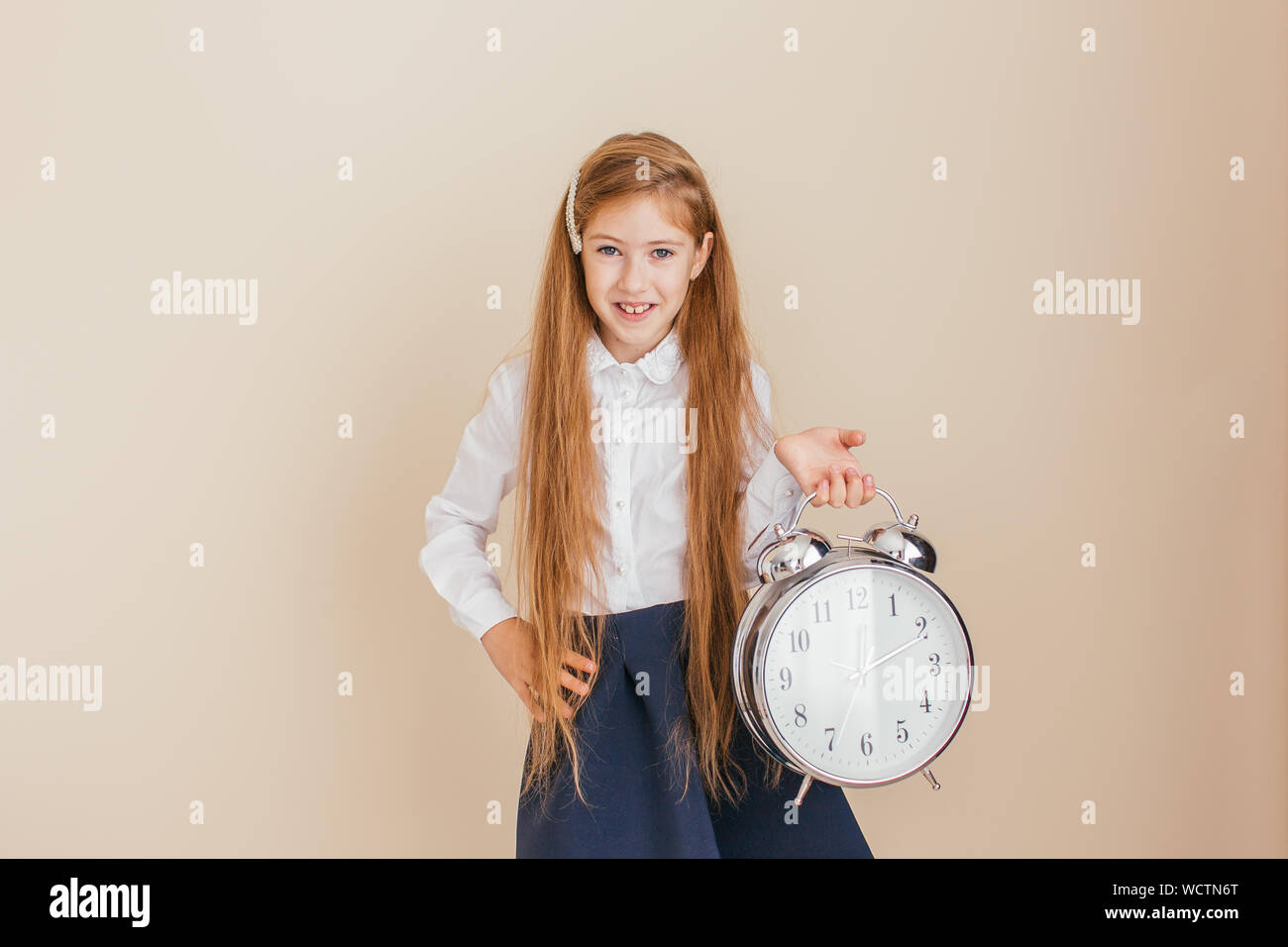 Smiling little girl with long hair holding big clock on neutral ...