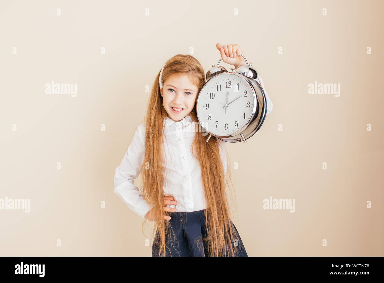 Smiling little girl with long hair holding big clock on neutral ...