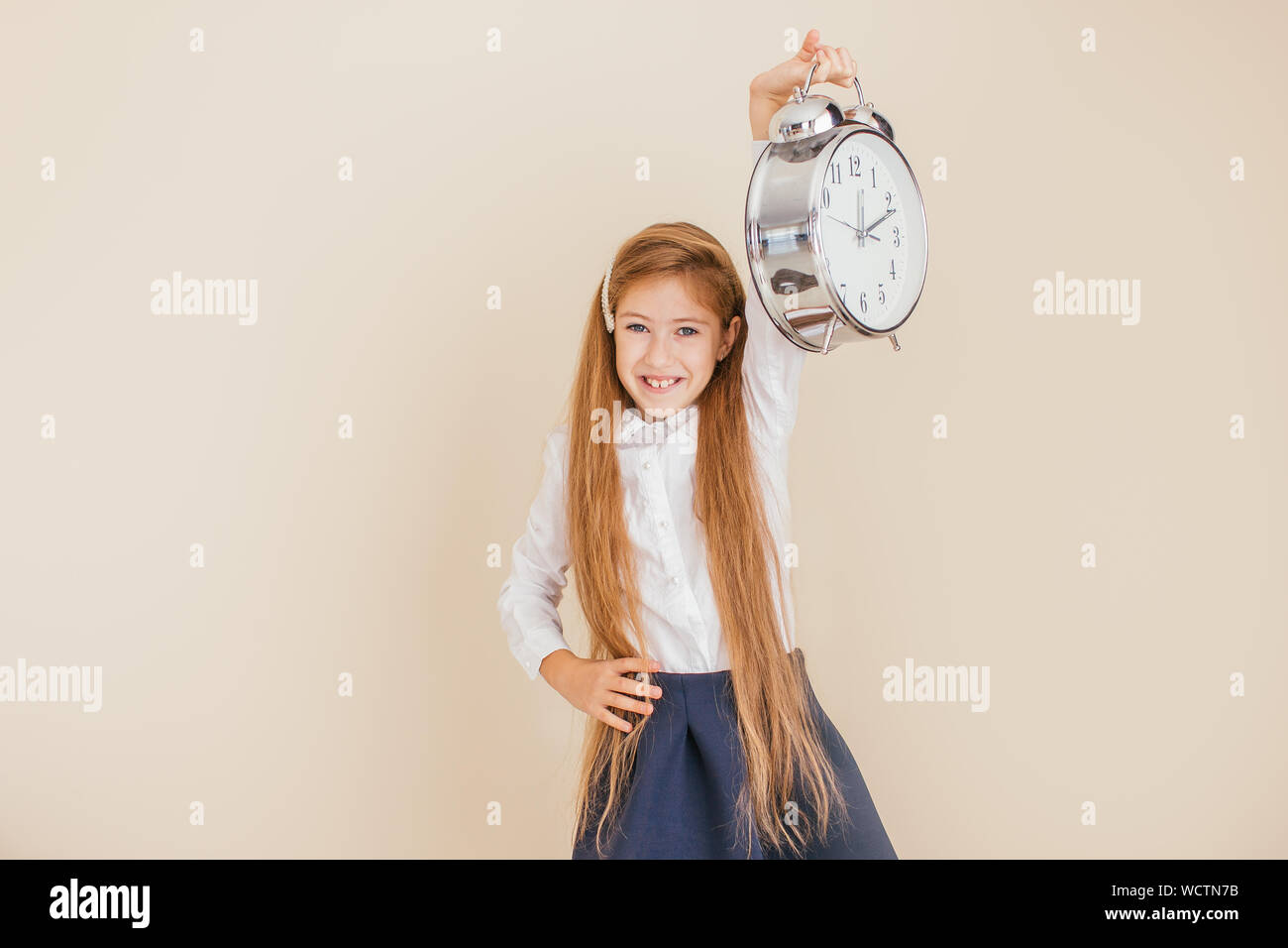Smiling little girl with long hair holding big clock on neutral ...