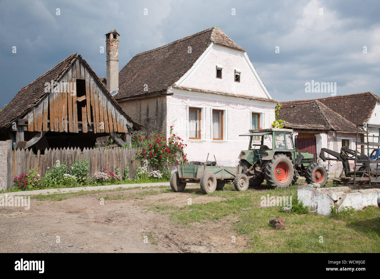 A dilapidated barn, a farmhouse and a tractor with trailer, in the ...