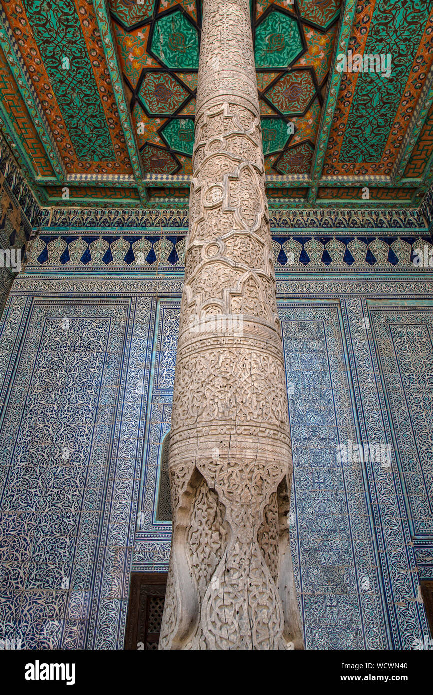 A traditional carved wooden pillar and blue mosaic tiles, on a mosque ...