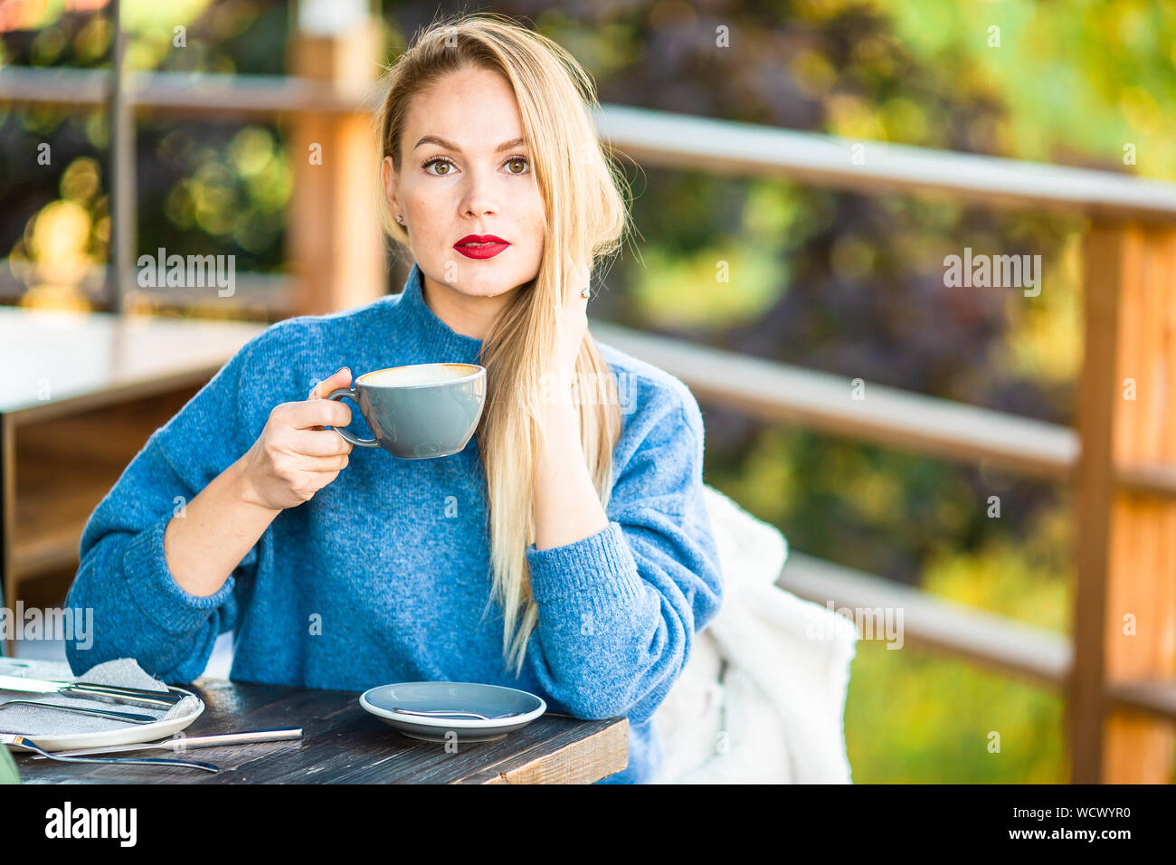 Beautiful blonde girl drinks hot coffee in outdoor cafe Stock Photo - Alamy