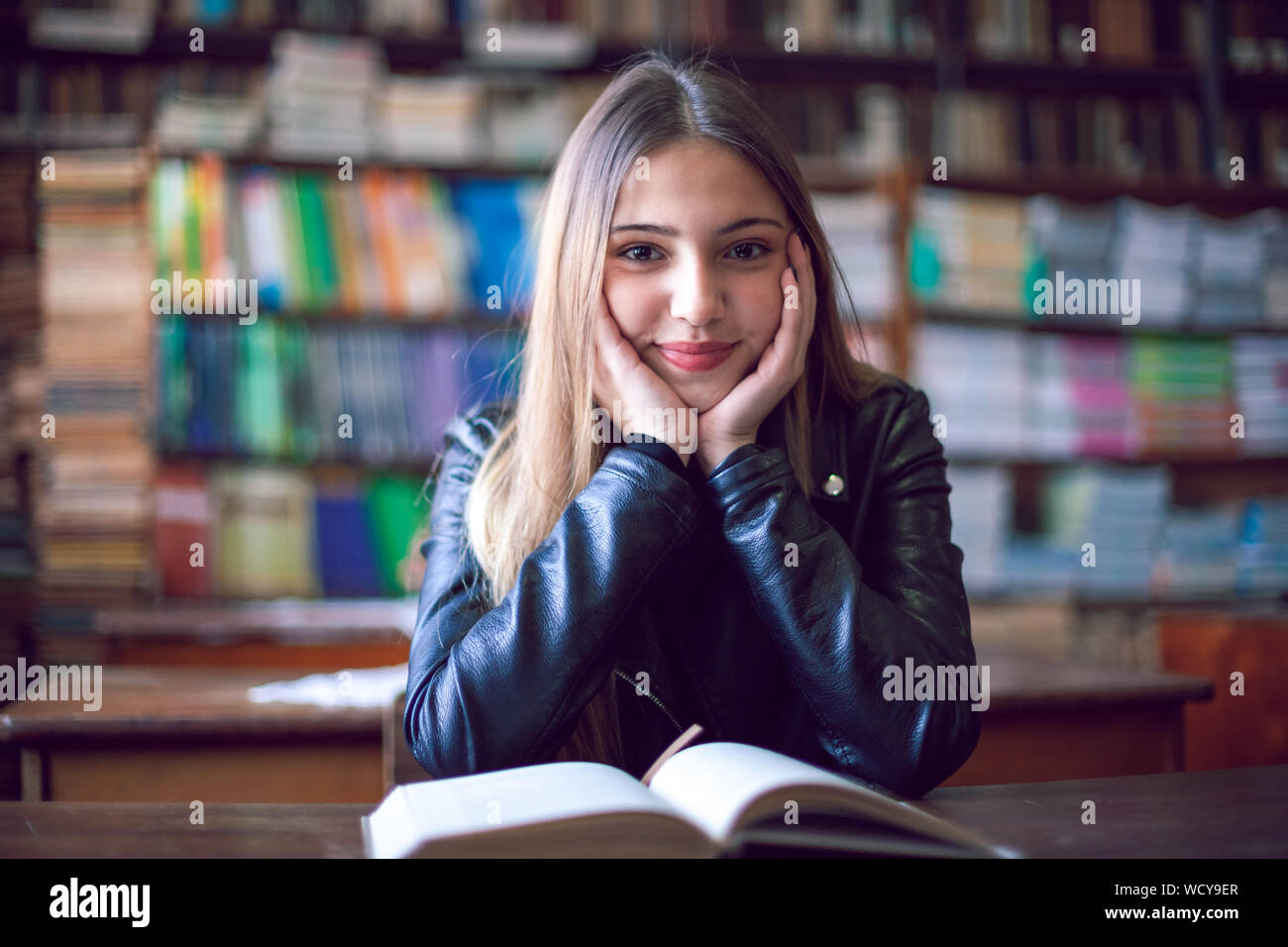 Beautiful teenager schoolgirl sitting in the library and reading a book ...
