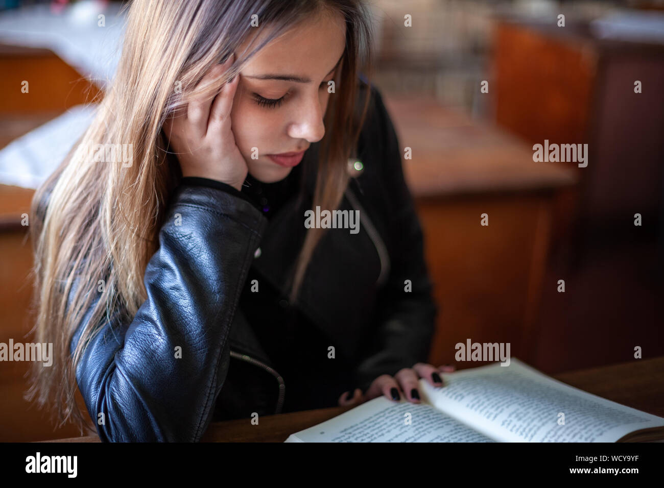 Beautiful teenager schoolgirl sitting in the library and reading a book ...