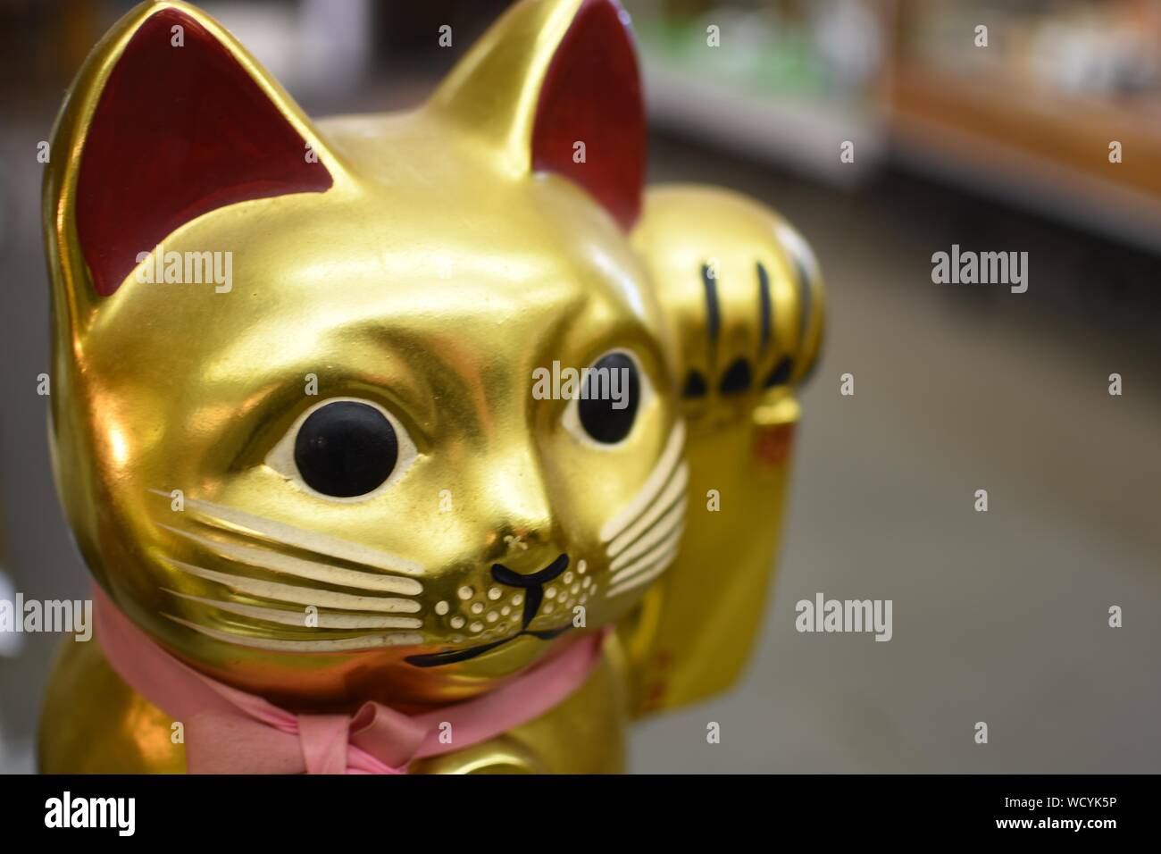 Cute selective closeup shot of a golden cat statue with a pink ribbon ...
