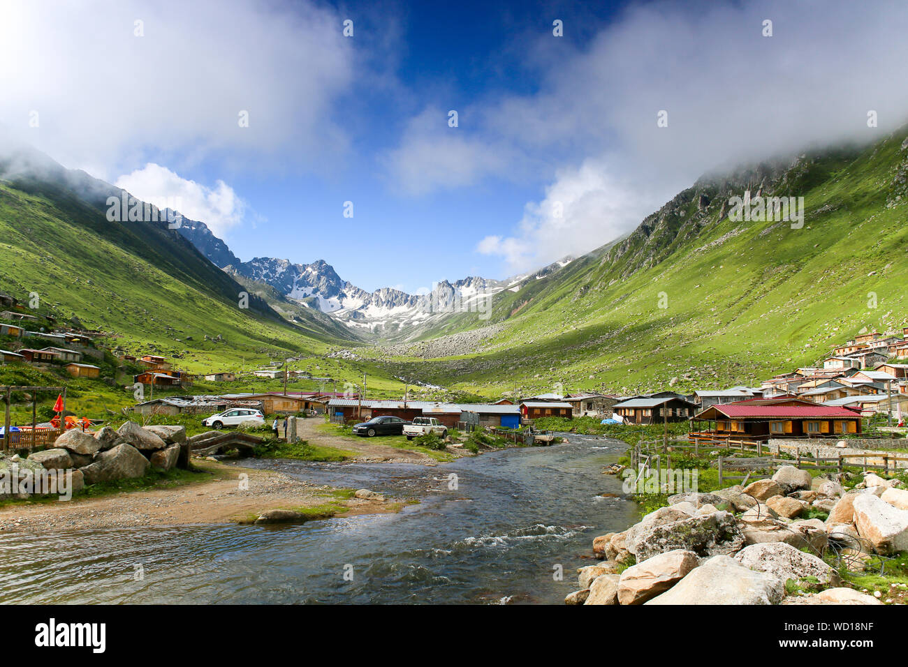 Village houses on the foreground, hills covered by clouds and a river ...