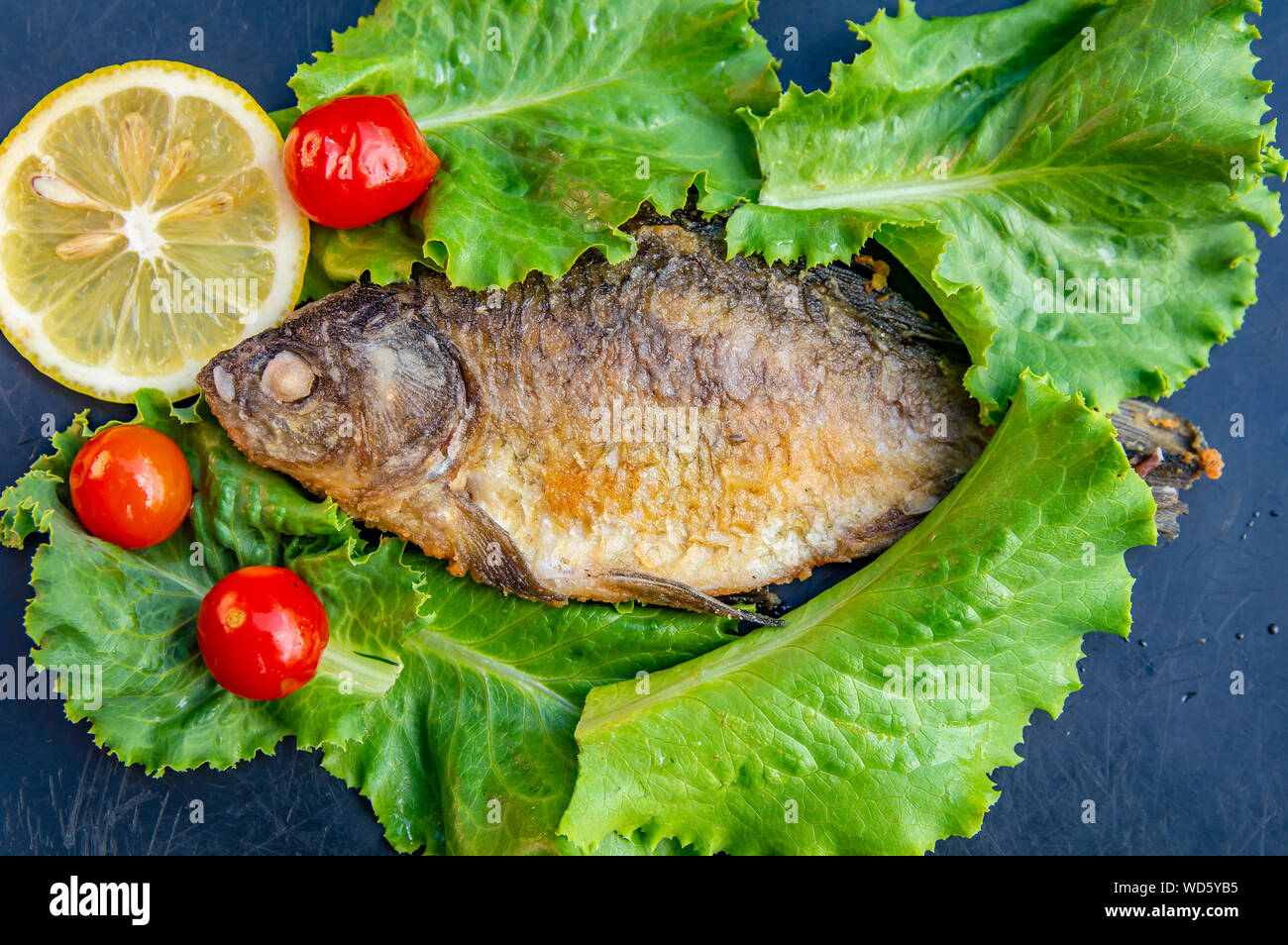 Fried crucian fish on a black background with vegetables and lemon ...