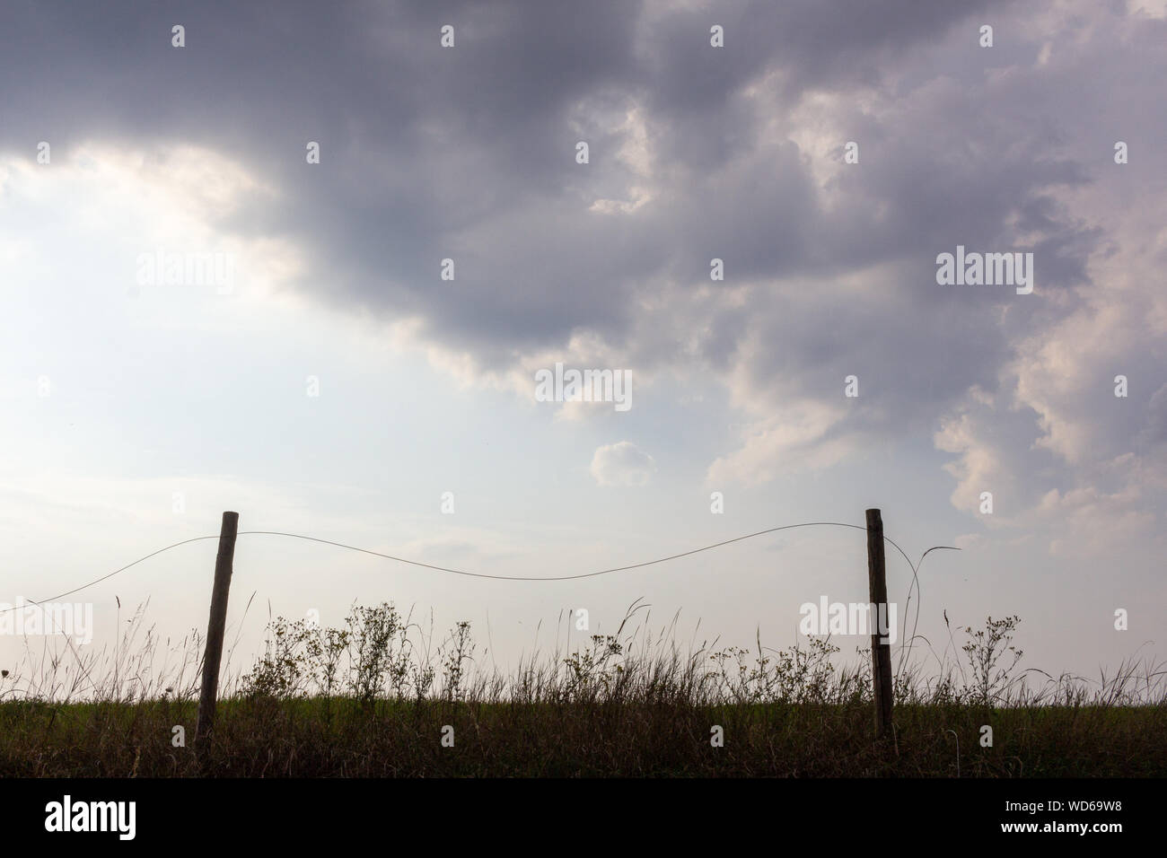 A single strand of wire runs between two posts against dark clouds ...
