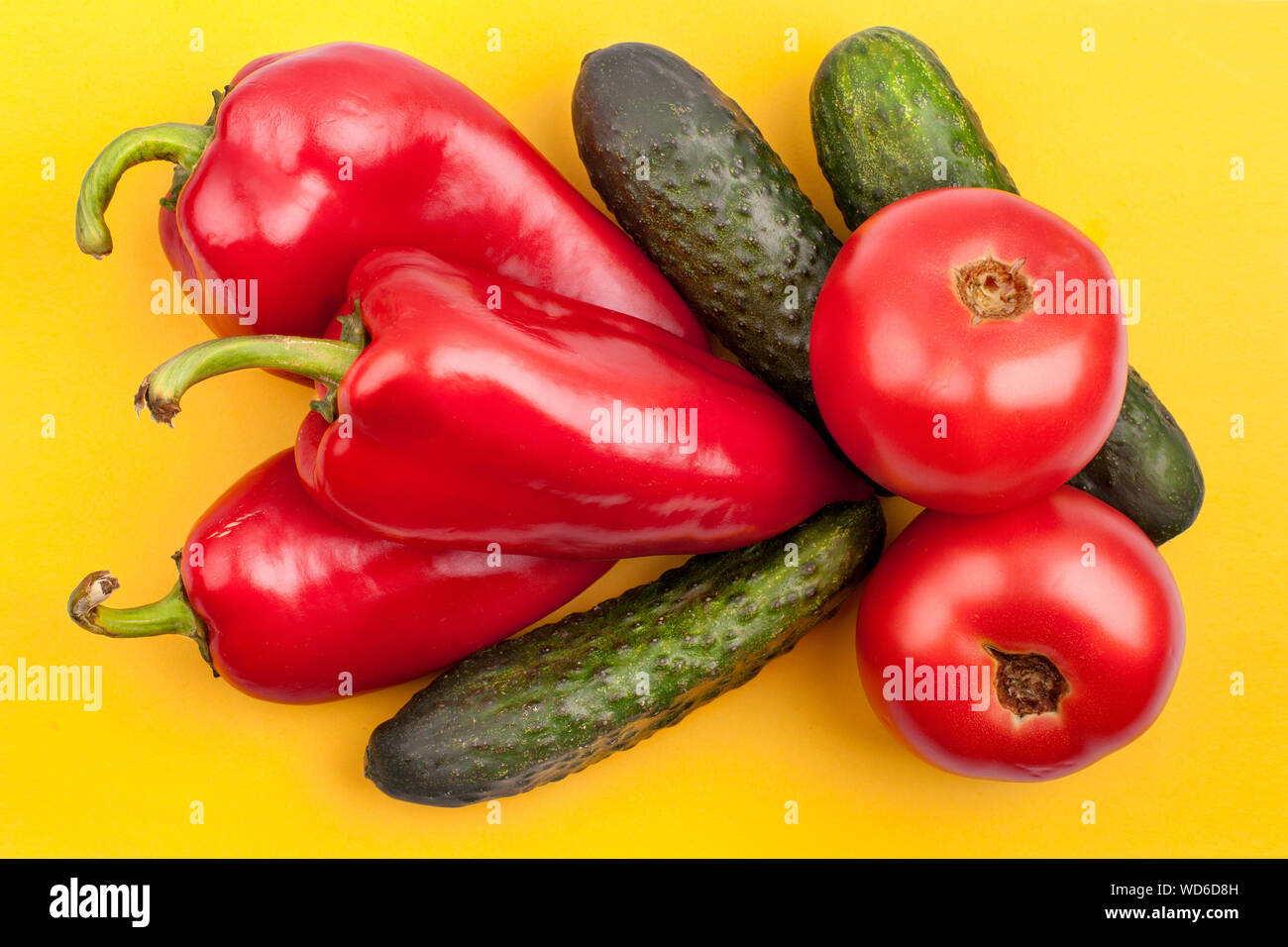 Bright red peppers, red tomatoes and green cucumbers on a yellow ...