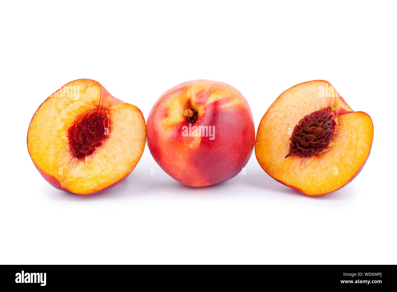 One peach and two halves of a peach with a stone on a white background ...