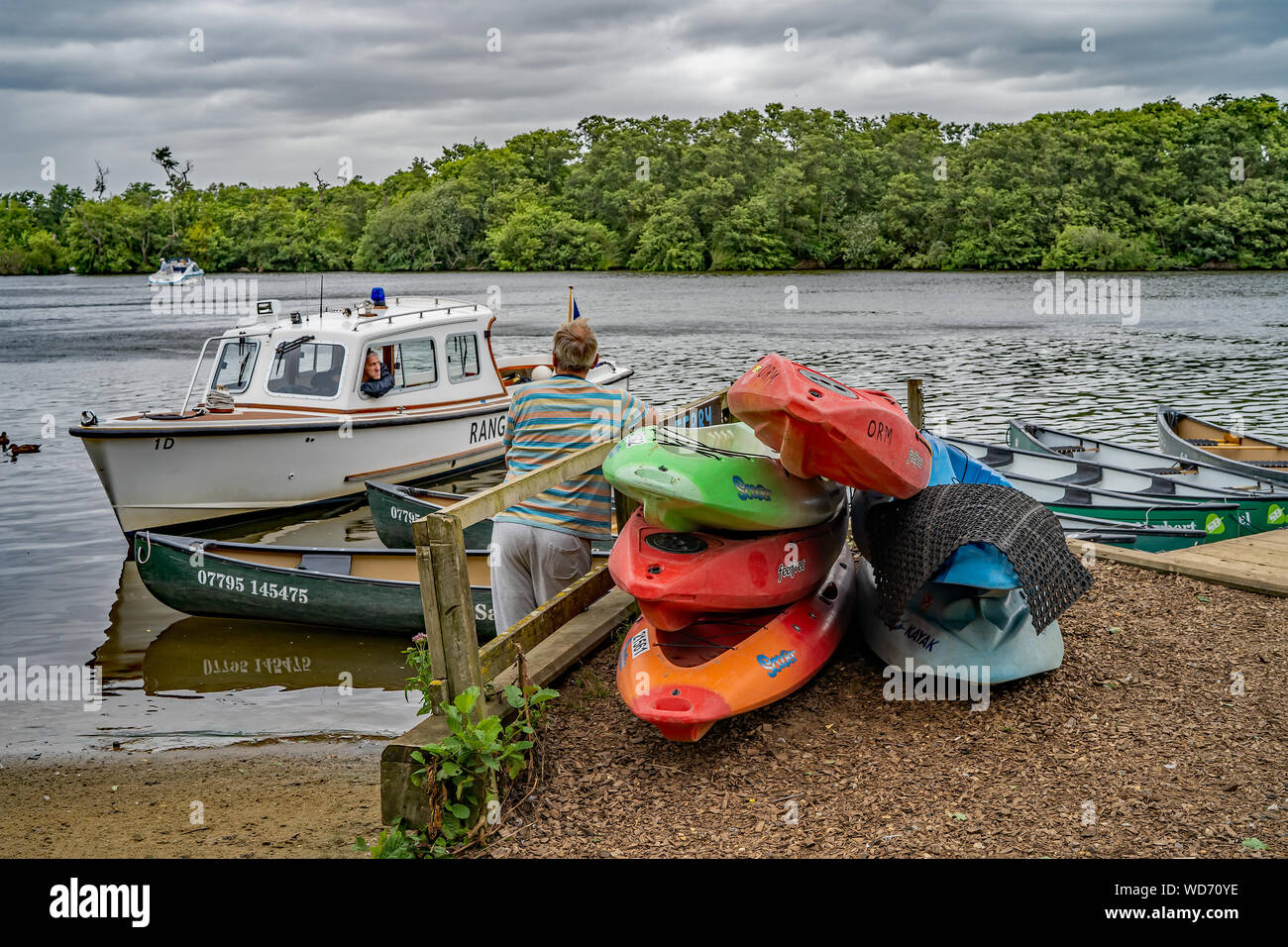 Man standing beside colorful hire canoes talking to a Norfolk Broads ...