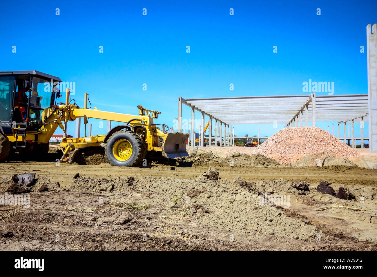 Operator is driving yellow grader, leveling ground at building site ...