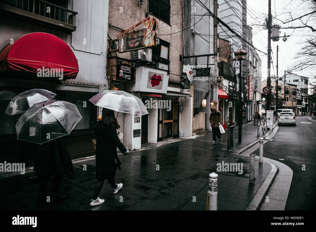 Wide shot of people with umbrellas walking on a pedestrian zone near ...