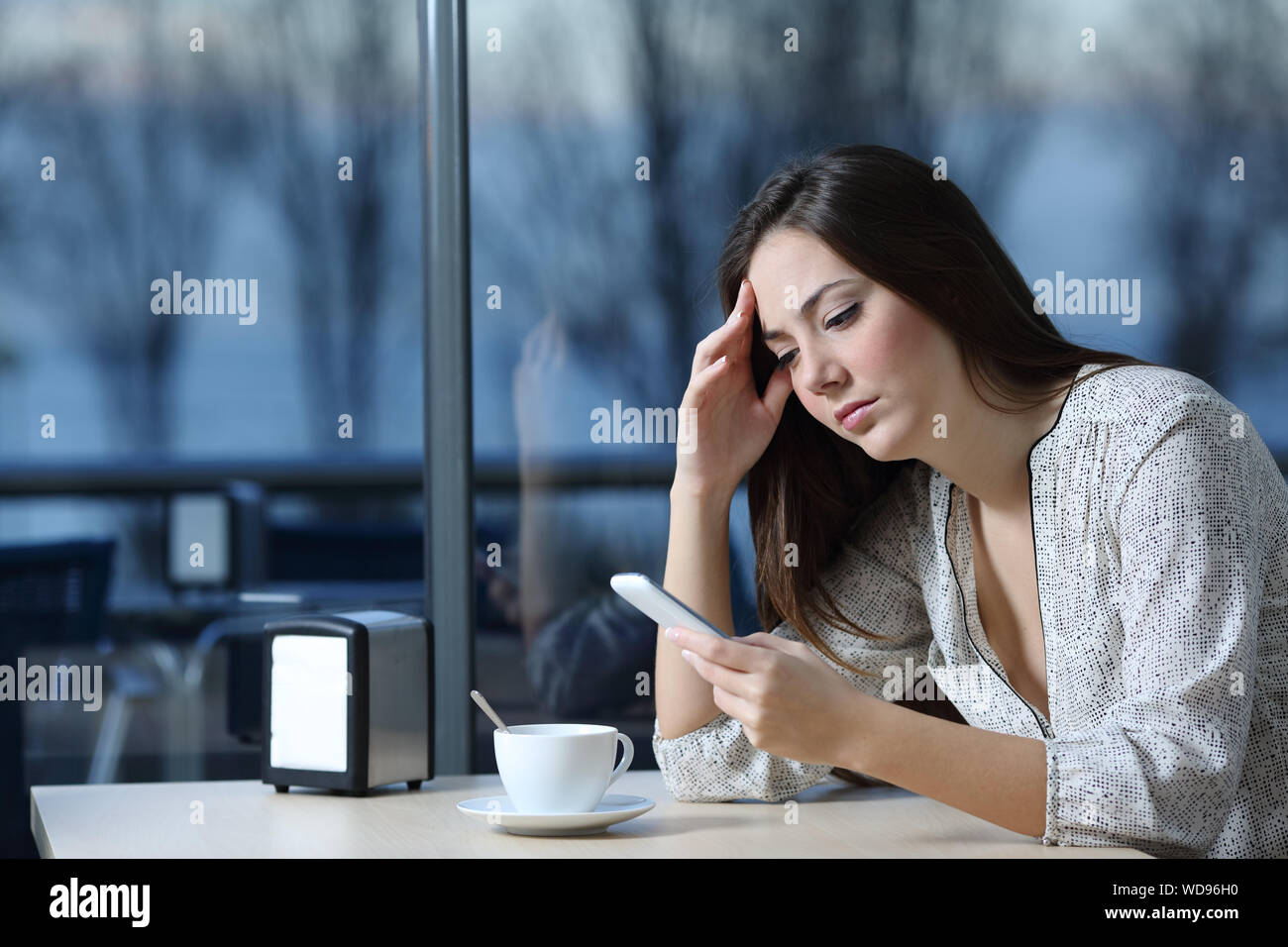 Worried girl checking phone message sitting in a coffee shop in a sad ...
