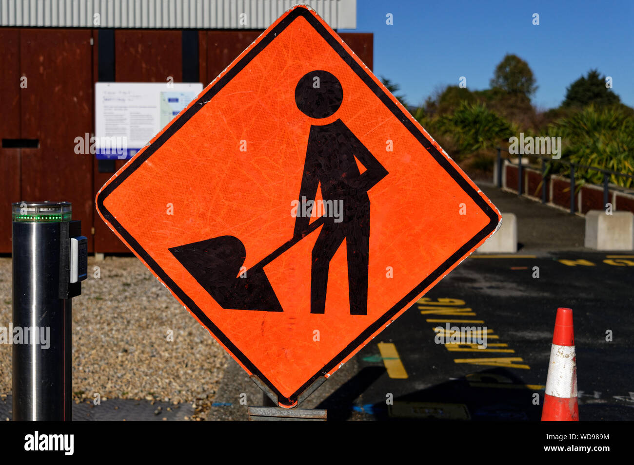 An orange diamond sign with a figure of a person at work warns of ...