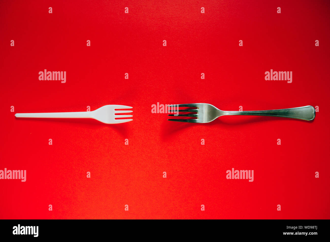 A plastic fork vs metal one on a red background. The concept of ...