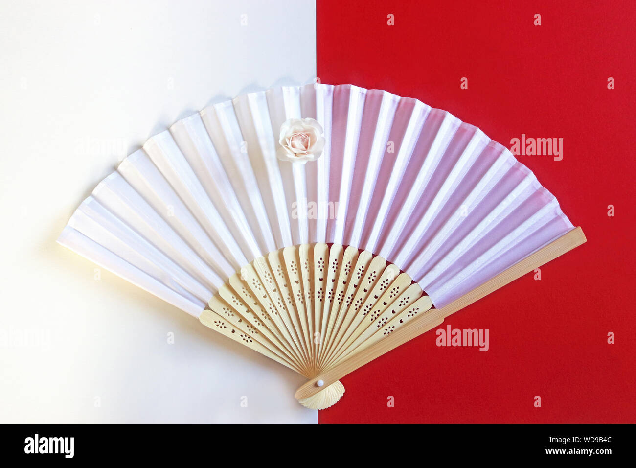 white hand fan with a rose on red and white background Stock Photo - Alamy