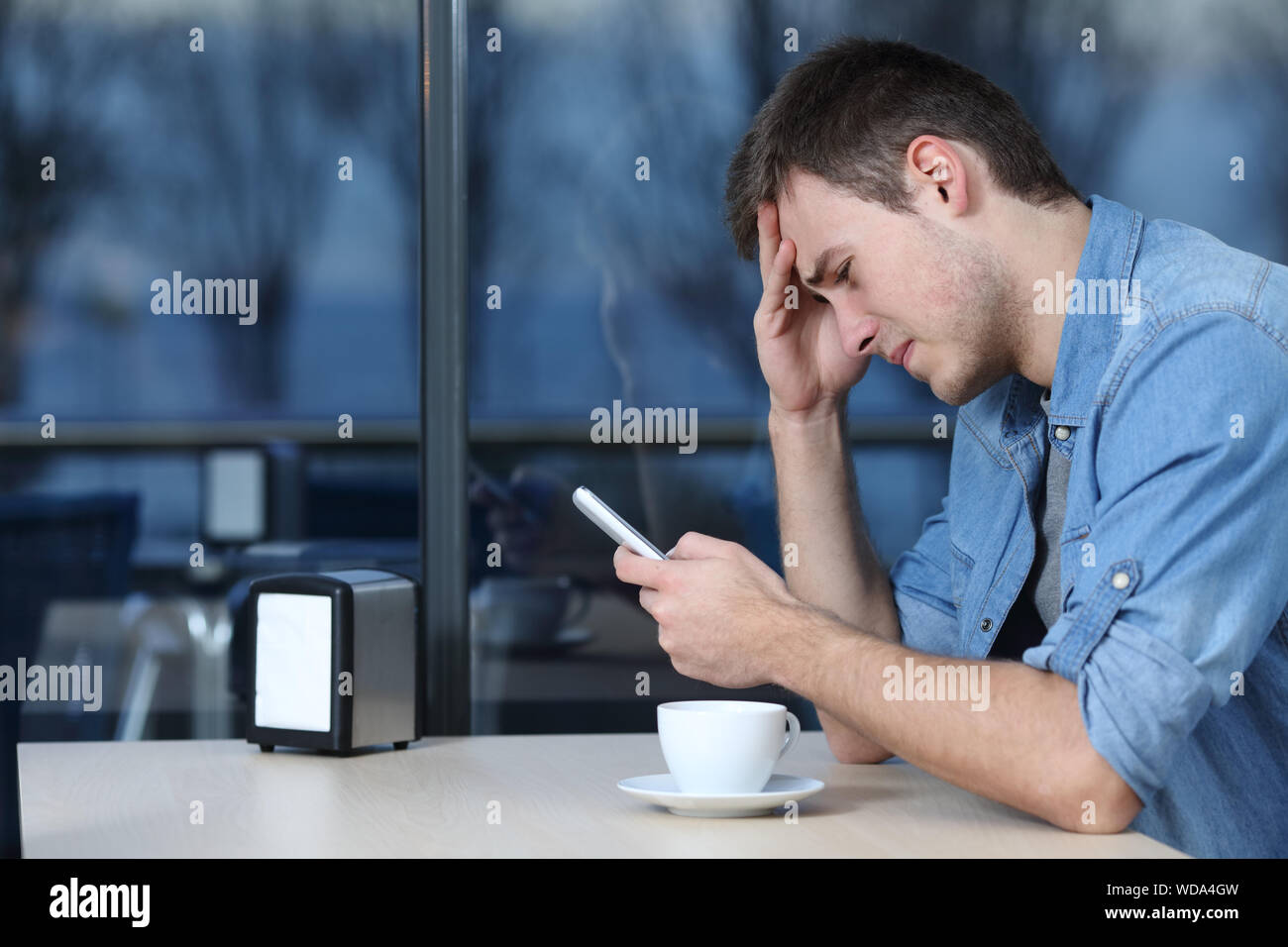 Side view portrait of a sad man checking mobile phone message in a ...