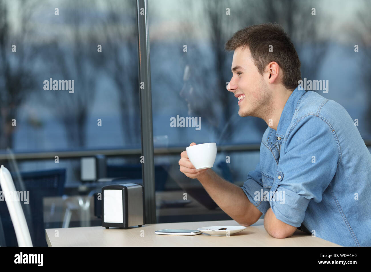 Happy man looking outdoors through a window holding a cup in a coffee ...