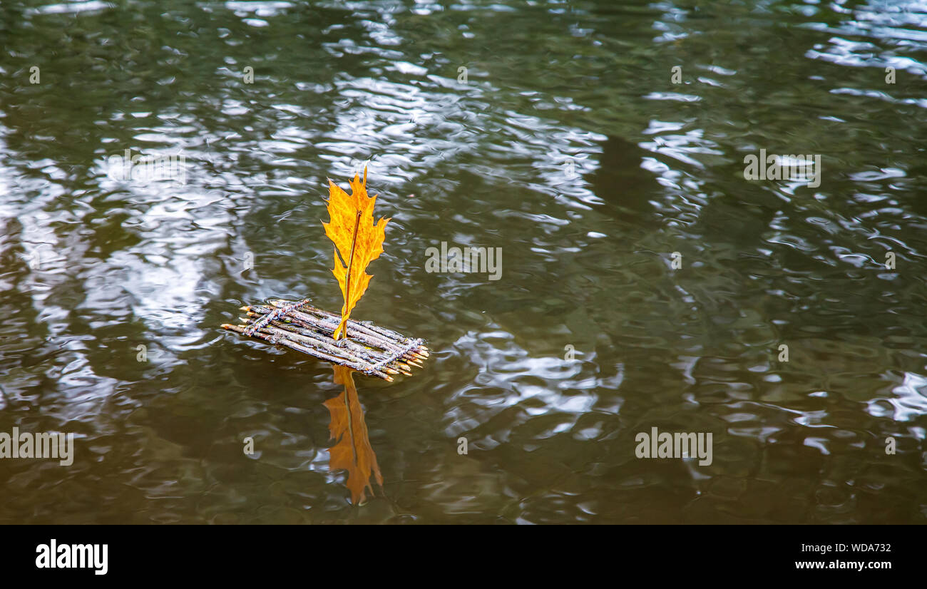 toy raft with a sail from maple leaf floating on the lake on autumn day ...
