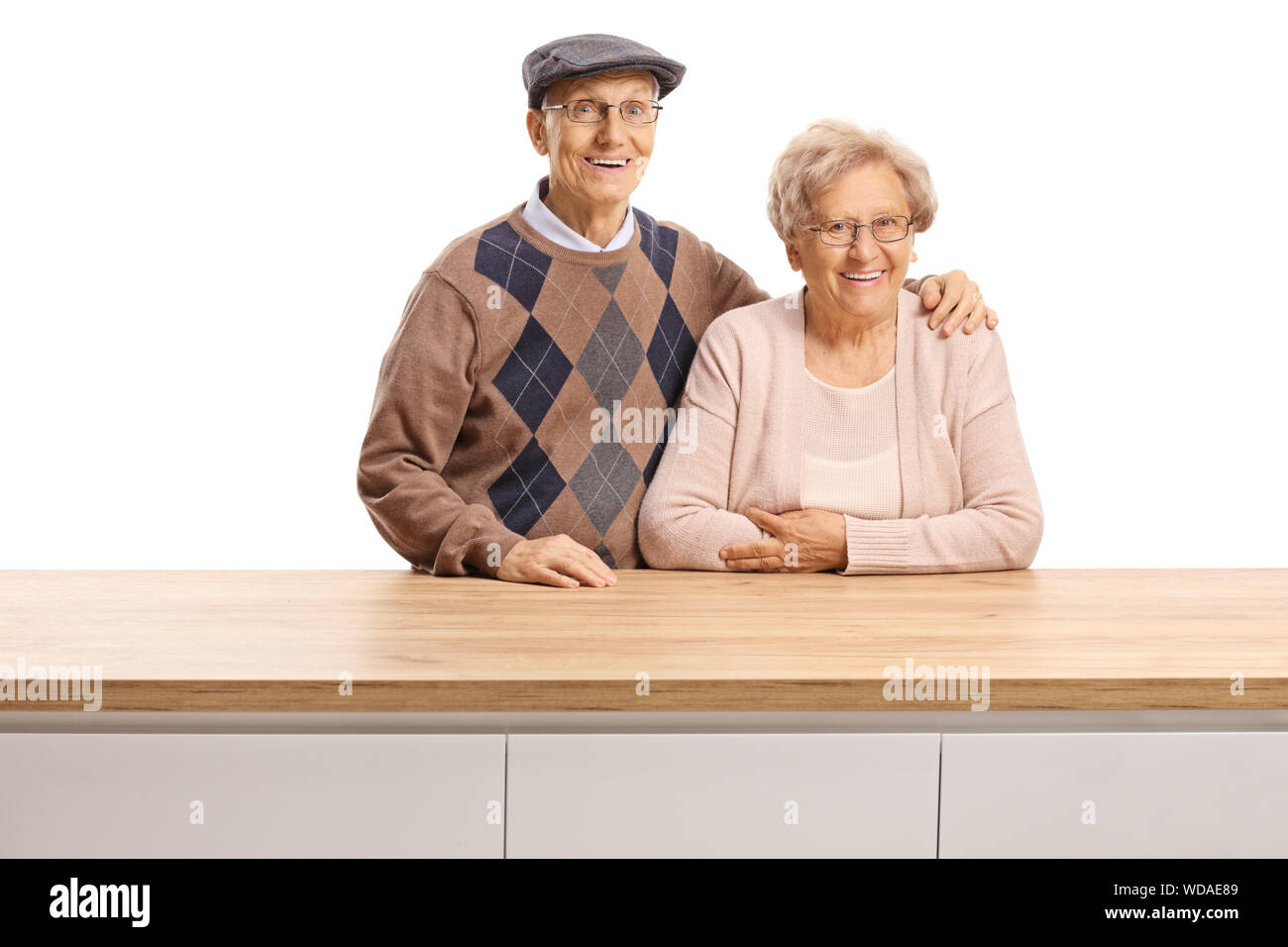Elderly man and woman posing behind a wooden counter isolated on white ...