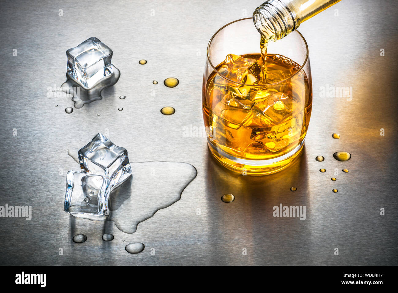 Pouring whisky into glasss with ice on metallic background close up ...