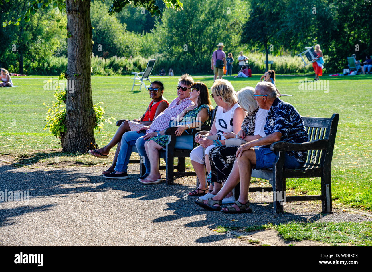 Friends sit together on benches in a park at Marlow, Buckinghamshire ...