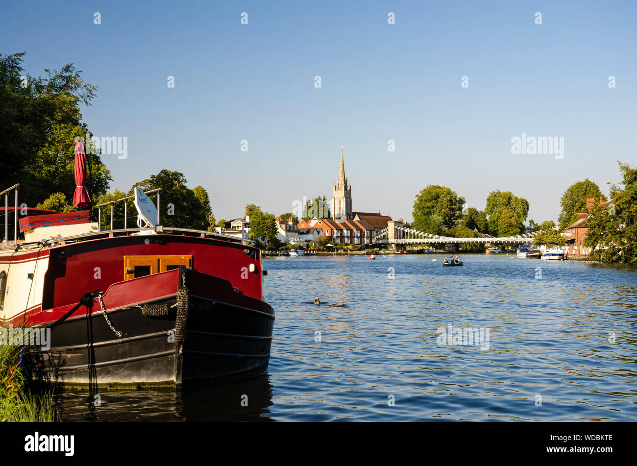 A red narrowboat moored on the bank of The River Thames next to the ...