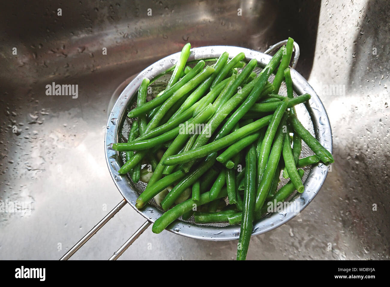 Washed raw green beans in mesh strainer in sink of kitchen, top view ...
