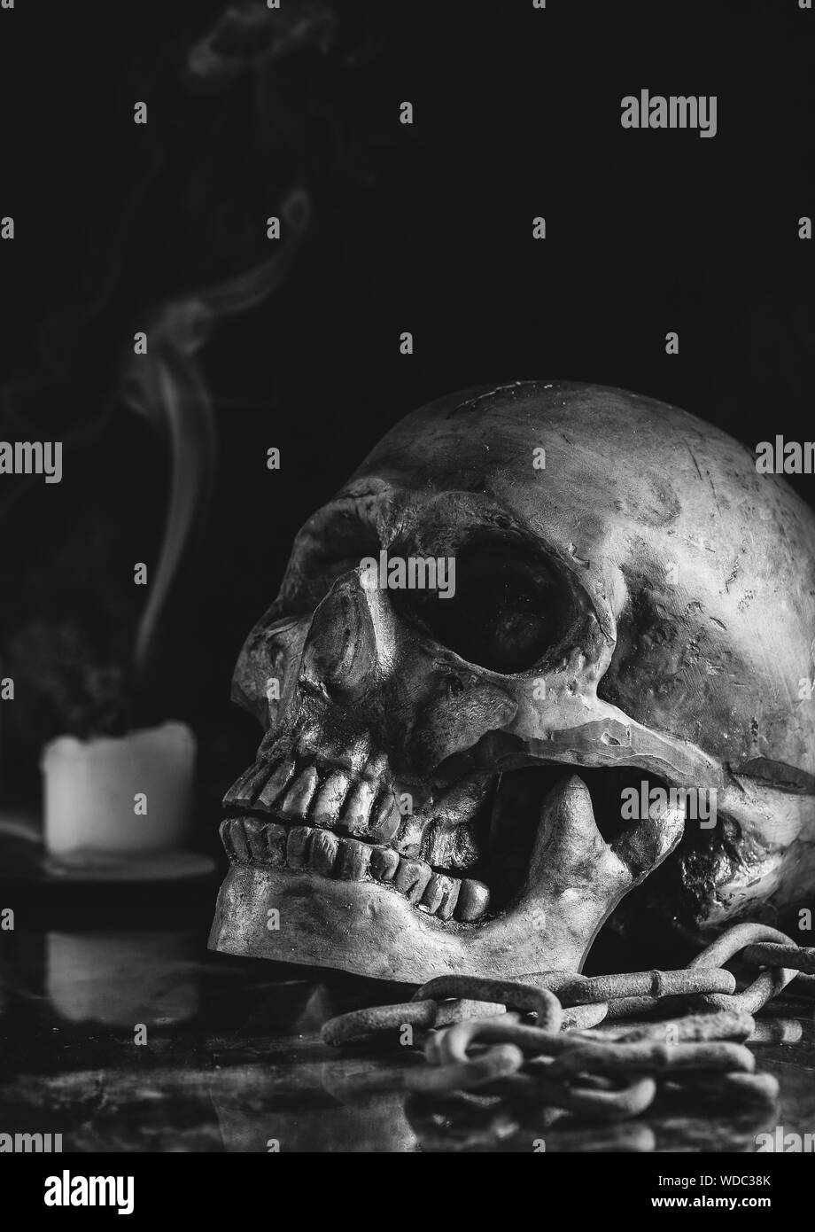 Closeup of a scary human skull with smoldering candle in background ...